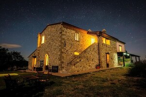 Edifício de pedra com várias janelas e varanda coberta, iluminado por luzes quentes.