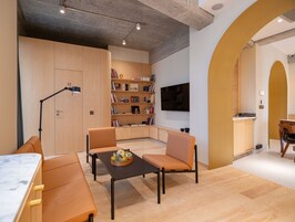 Uma sala de estar moderna com um sofá, uma mesa de centro com uma cesta de frutas, uma estante de livros e uma TV na parede.