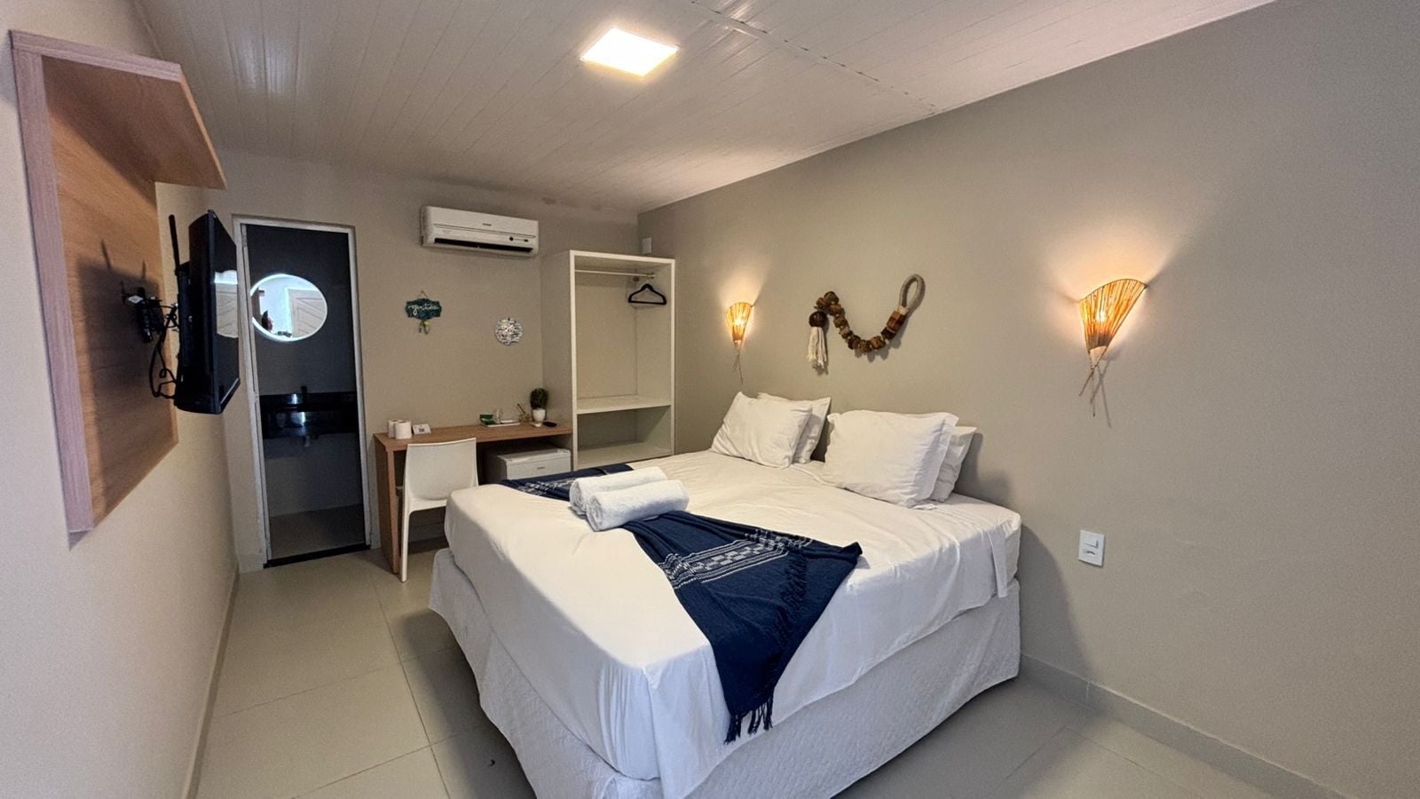 Um quarto com cama, mesas de cabeceira, escrivaninha, cadeira e guarda-roupa.