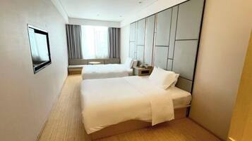 Quarto de hotel moderno com uma cama grande, uma cama menor, uma TV na parede e uma janela com cortinas.