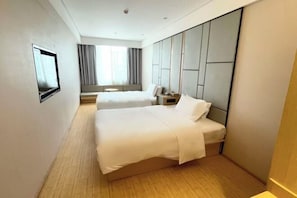 Quarto de hotel moderno com uma cama grande, uma cama menor, uma TV na parede e uma janela com cortinas.