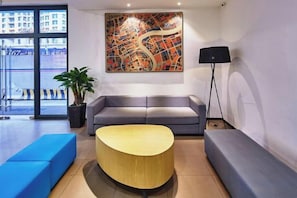 Um hall moderno com uma mesa de madeira curva, um sofá cinzento e um grande quadro abstrato na parede.