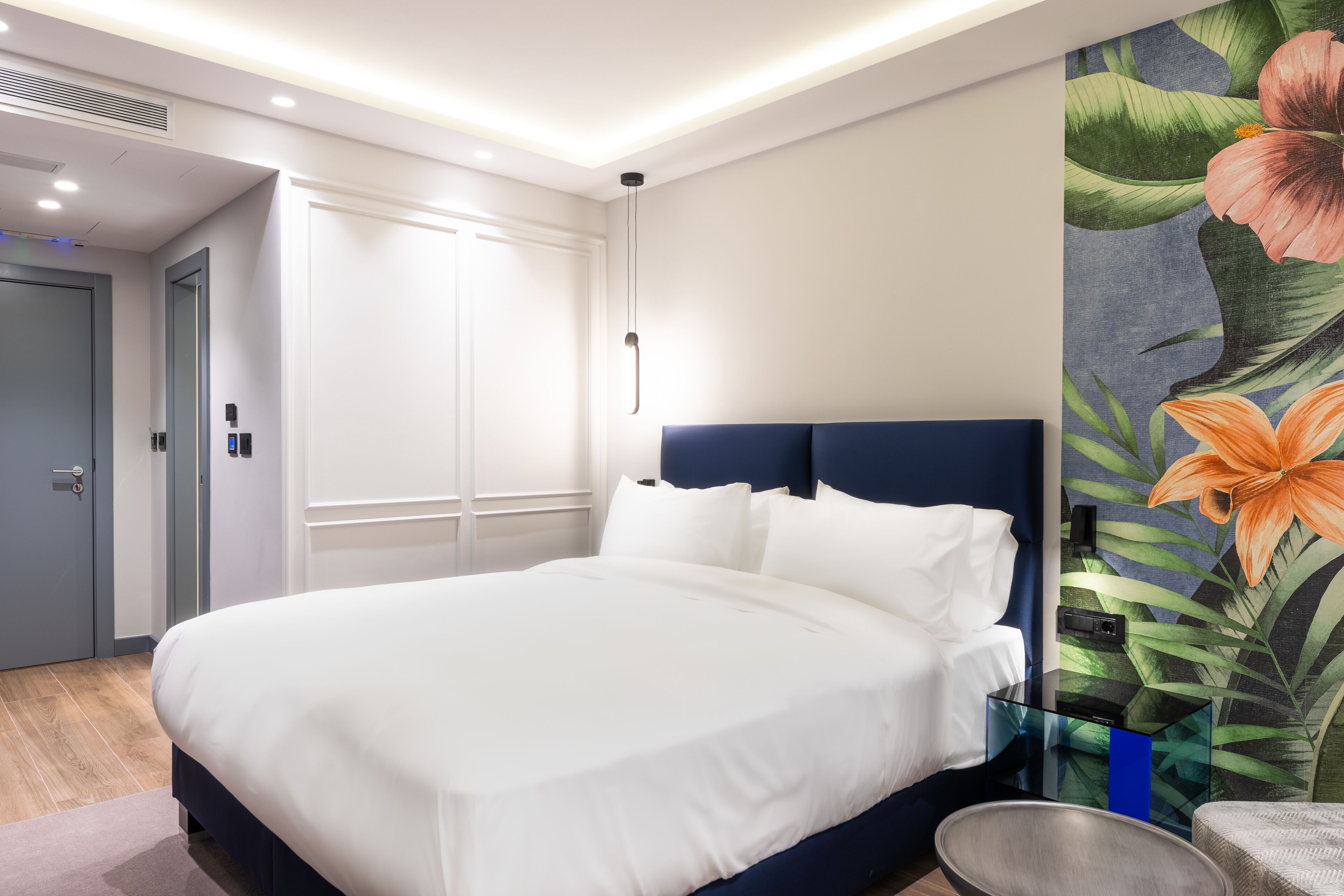Quarto moderno com uma cama grande, uma mesinha de cabeceira e uma luminária na parede.