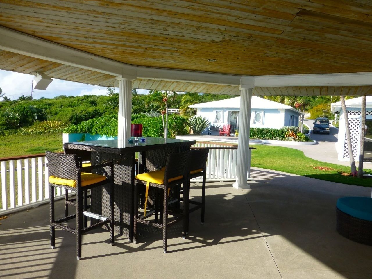 Um pátio coberto com mesa e cadeiras, vista para uma área residencial e um cercado branco.
