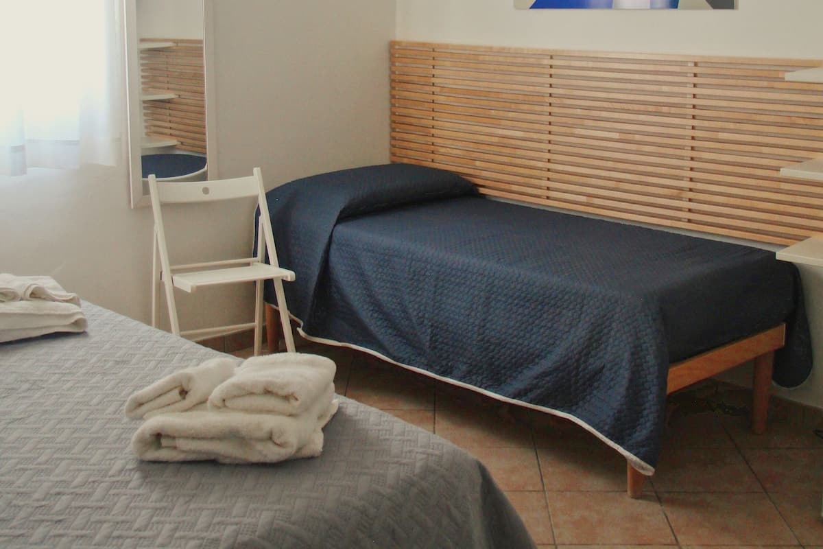 Quarto com cama, cadeira, mesa de cabeceira, espelho e uma obra de arte na parede.