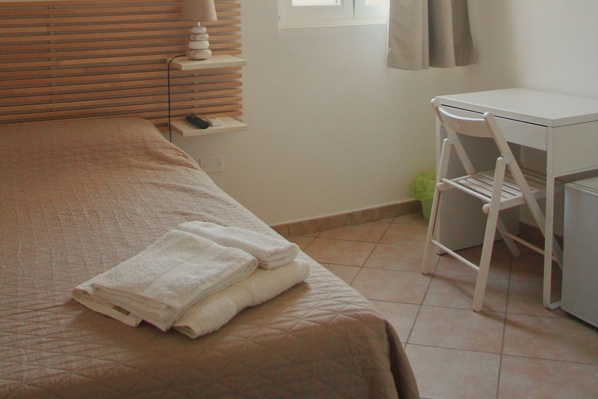 Quarto com cama, escrivaninha e janela com cortinas.