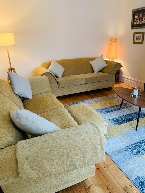 Uma sala de estar com sofá, poltronas, mesa de centro, luminária e tapete.