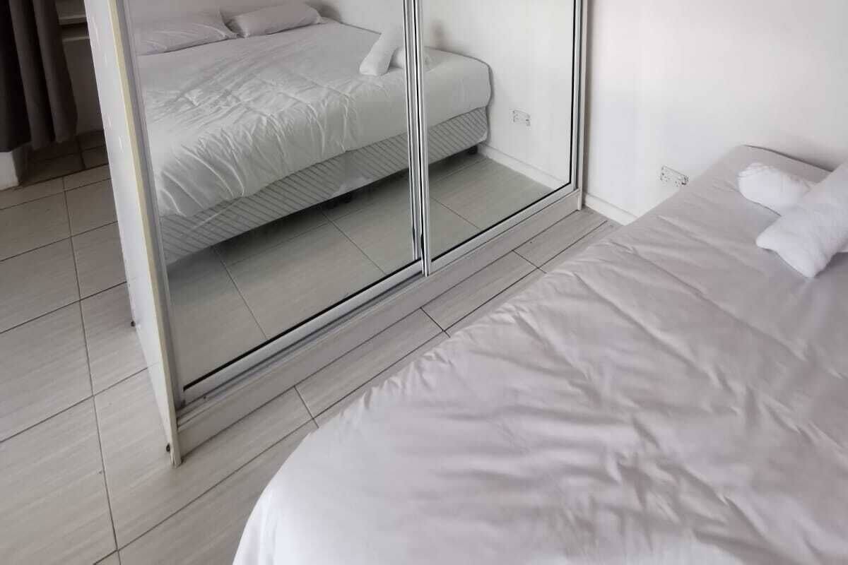 Quarto moderno com cama separada por divisória de vidro, cama individual e piso em azulejo.