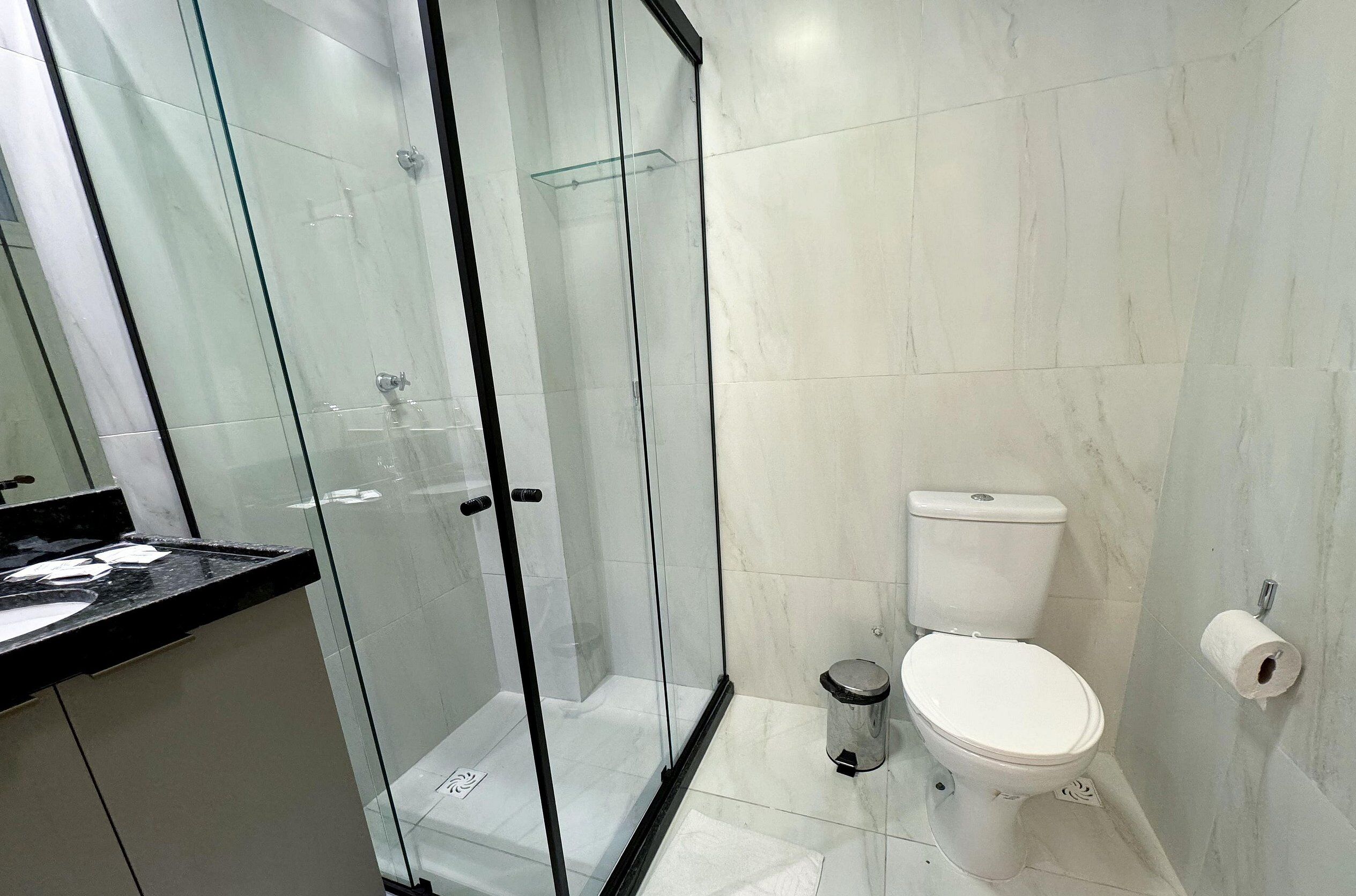 Uma casa de banho moderna com cabine de duche em vidro, sanita e lavatório com bancada preta.