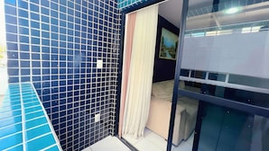 Um quarto com parede em azulejos azuis, uma porta de correr de vidro que dá para uma varanda e chão com azulejos brancos.