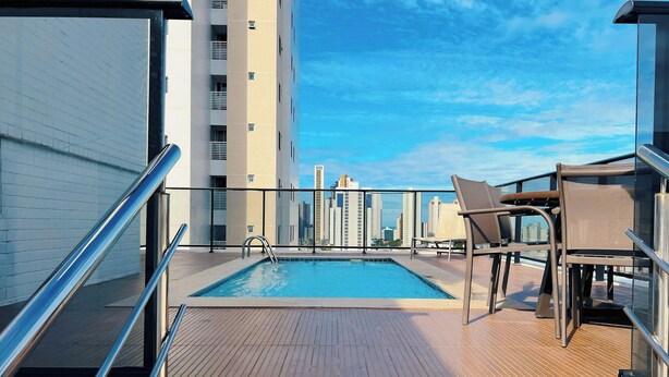 Uma área de piscina no terraço com vista para o horizonte da cidade, um deck de madeira e um espaço de estar com cadeiras e uma mesa.