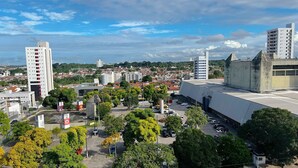 Paisagem urbana com um grande edifício industrial, vários edifícios altos e uma combinação de áreas verdes e carros estacionados.