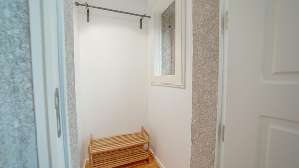 Um corredor estreito com um banco de madeira, um porta-toalhas e uma pequena janela.