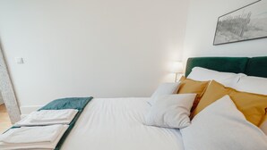 Uma cama bem arrumada com roupa de cama branca e verde, cabeceira verde e travesseiro branco.