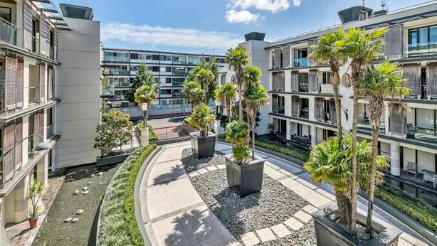 Um moderno conjunto de apartamentos com várias varandas, um pátio central com palmeiras e céu claro.