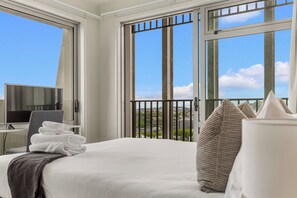 Quarto de hotel com cama, uma escrivaninha com computador e janela com vista para a cidade.