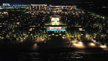 Um hotel grande com vários andares, um pátio central com piscina e árvores ao redor.