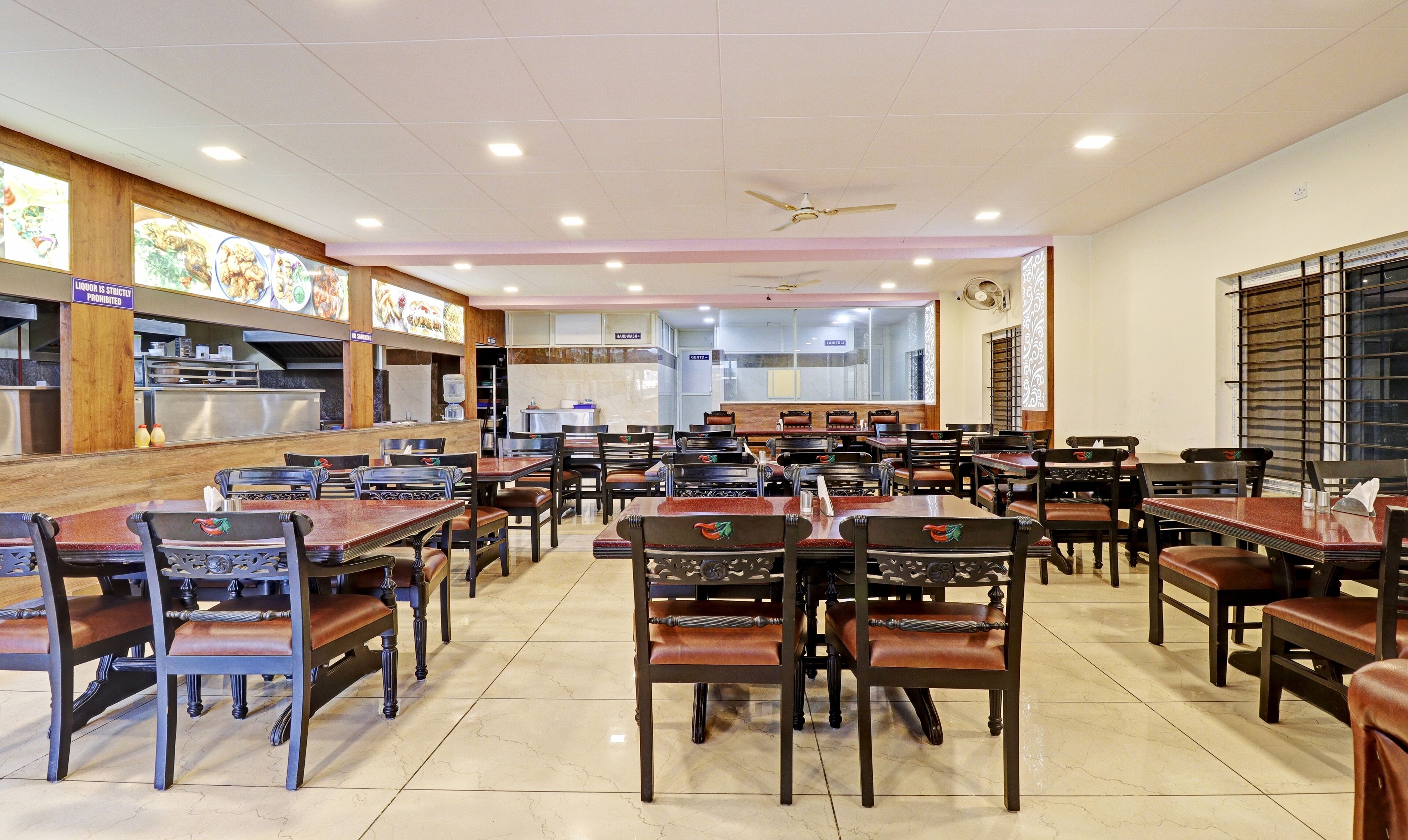 Um restaurante amplo com várias mesas e cadeiras, uma área de cozinha e um ventilador de teto.