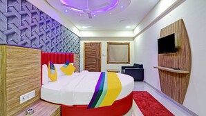 Quarto moderno com cama curva, televisão fixada em painel de madeira e ventilador de teto com iluminação roxa.