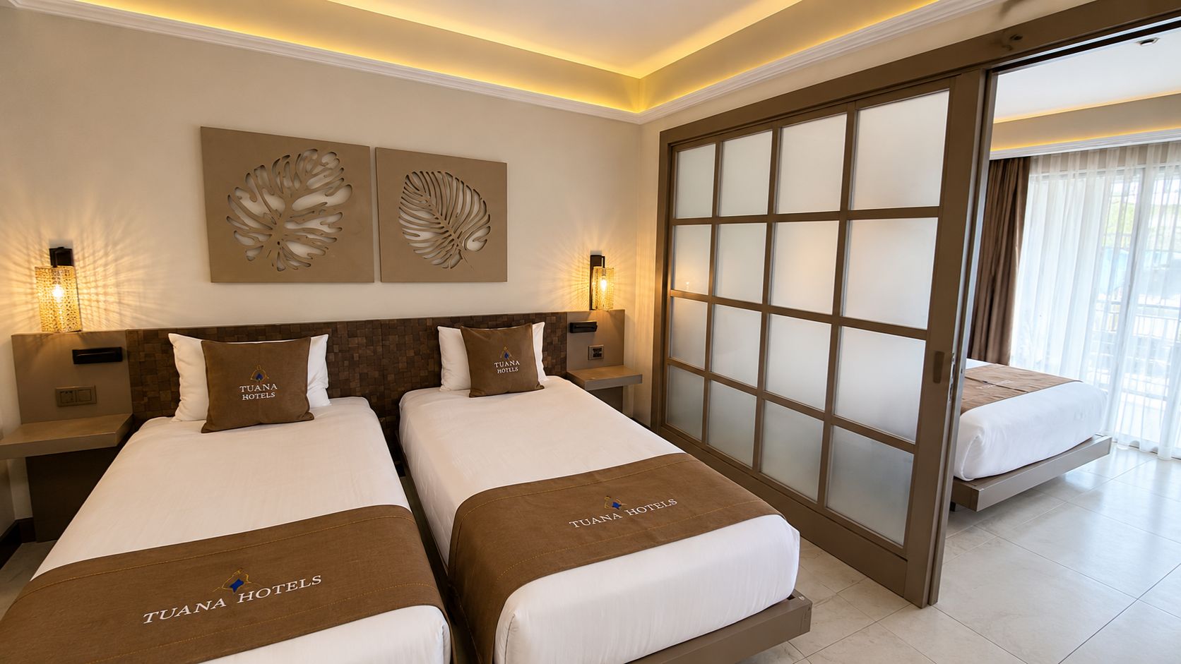 Quarto de hotel com duas camas, porta de vidro que se abre para uma varanda e arte decorativa na parede.