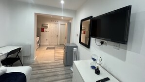 Quarto de hotel com cama, escrivaninha, cadeira, televisão, espelho e mesinha de centro com um vaso e um controle remoto.