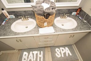 Casa de banho com duas pias, cesto de toalhas, artigos de higiene e um tapete com a inscrição 'BATH SPA'.