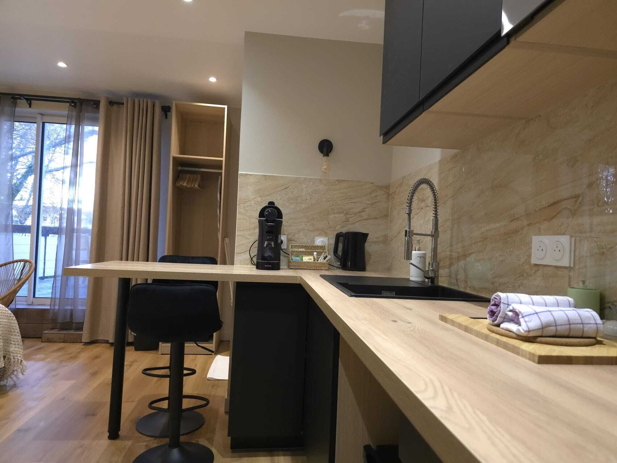 Uma cozinha moderna com bancada de madeira, banquetas pretas, cafeteira e pia com torneira flexível.