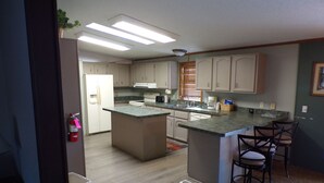 Uma cozinha com ilha central, banquetas, geladeira e cafeteira.