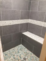 Um chuveiro com azulejos escuros, um nicho branco salpicado e um chão com padrão de folhas.