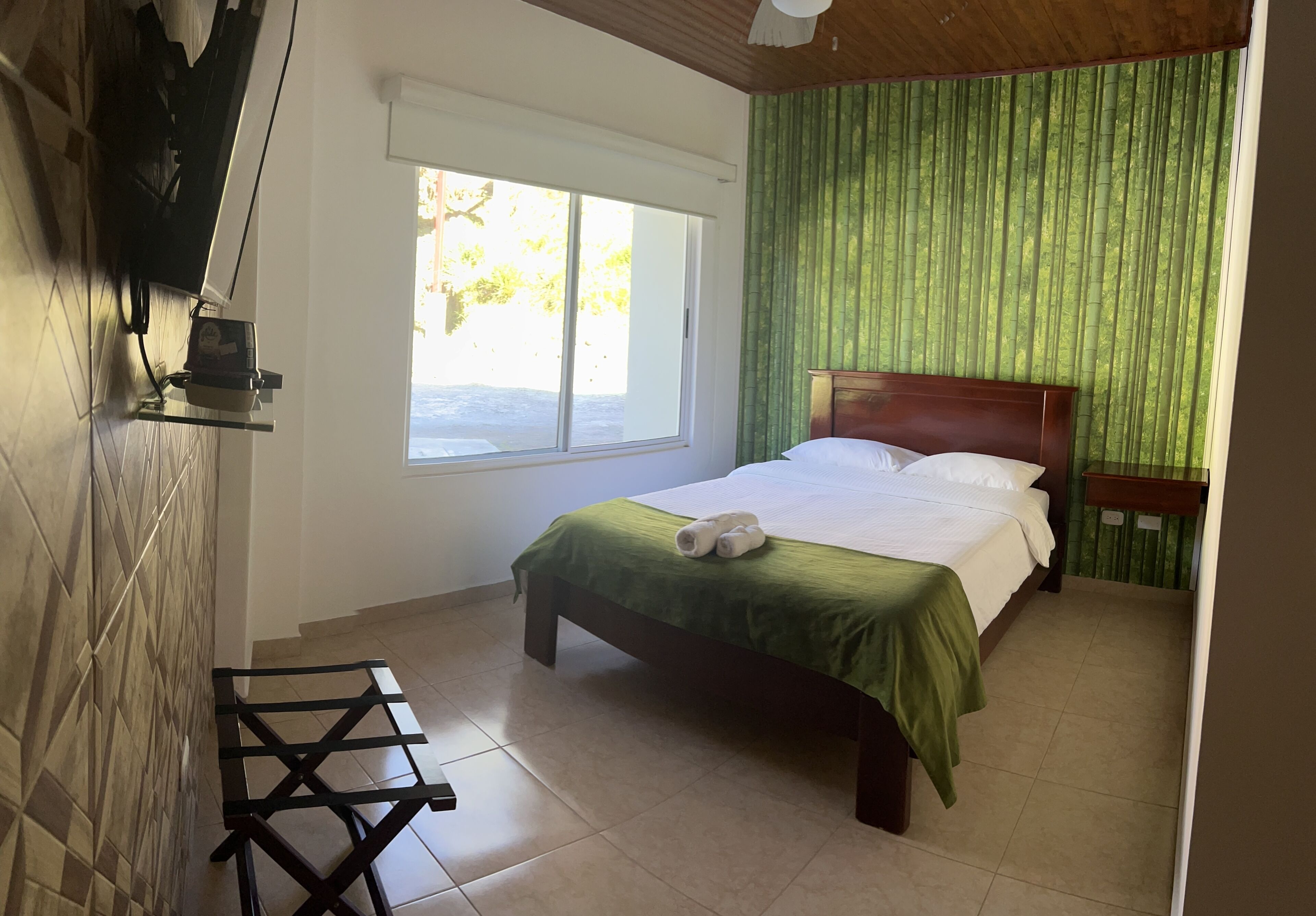 Quarto com cama, janela, cortina verde e cabeceira de madeira.