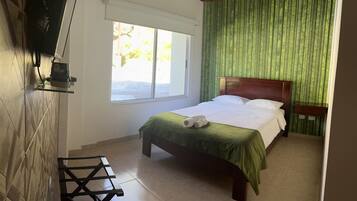 Quarto com cama, janela, cortina verde e cabeceira de madeira.