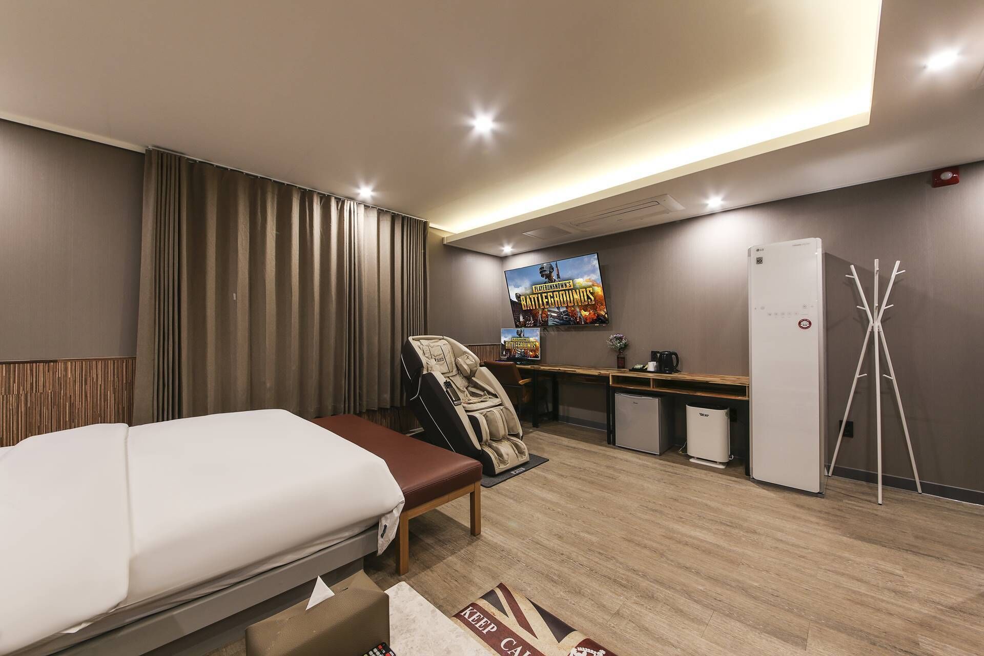 Quarto de hotel com cama, escrivaninha, cadeira, televisão e frigorífico.