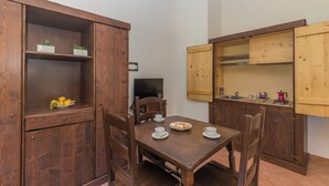 Cozinha compacta com armários de madeira, uma mesa de jantar e cadeiras. Há duas pequenas plantas em vasos numa prateleira, uma tigela de limões e um prato de biscoitos na mesa.