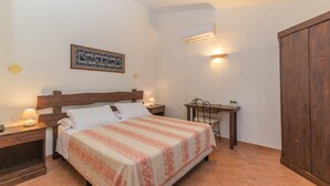 Quarto com cama, mesas de cabeceira, escrivaninha, ar condicionado e guarda-roupa.