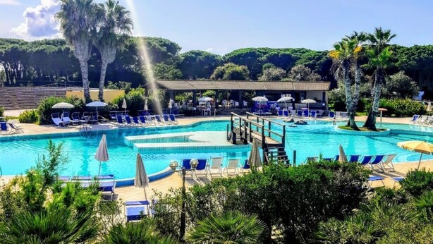Uma área de piscina com várias seções, espreguiçadeiras, guarda-sóis e palmeiras.