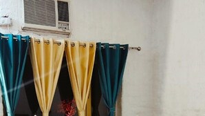 Quarto com piso de madeira, sofá, cama, ventilador de teto e cortinas.
