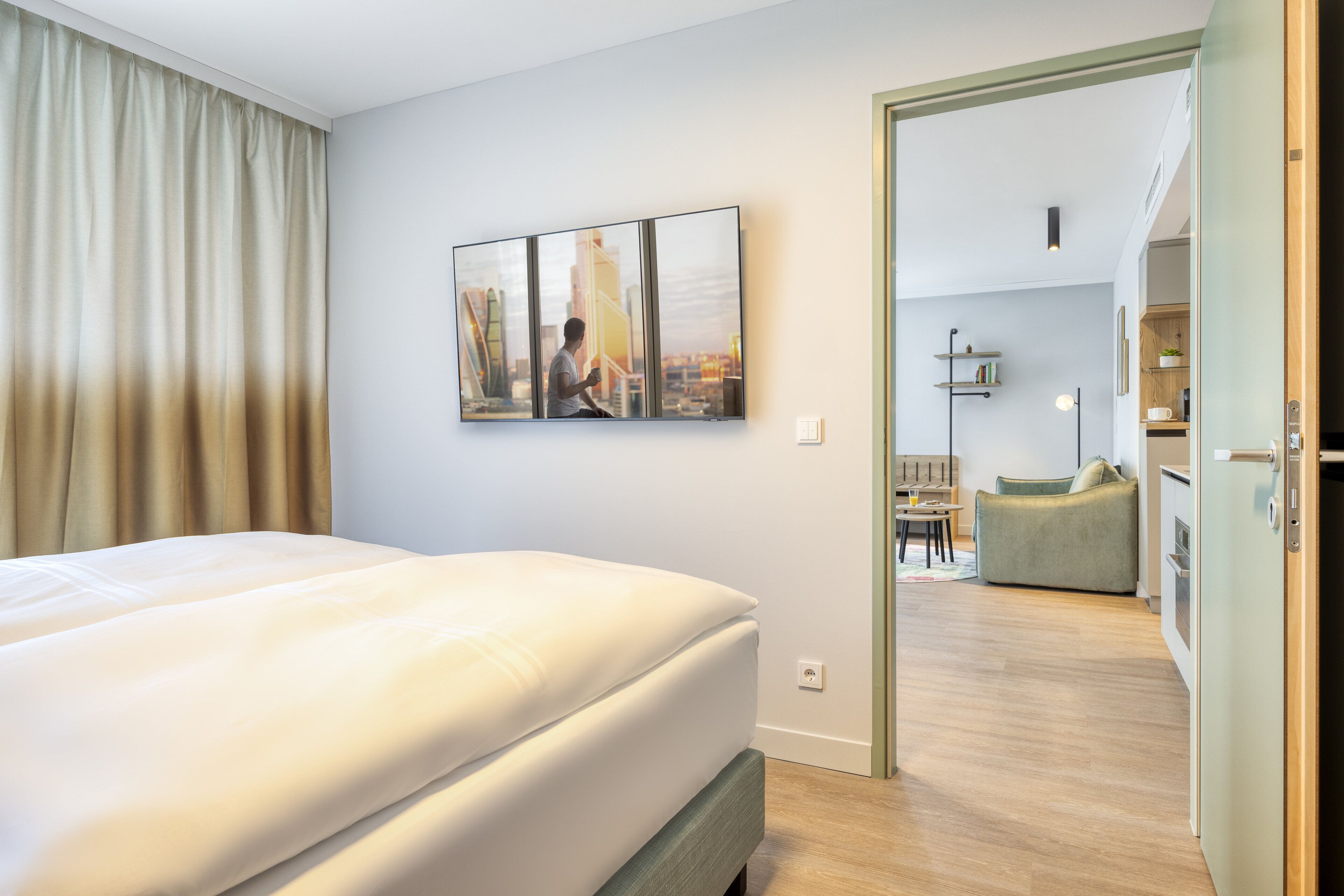 Quarto de hotel com cama, vista para a cidade, área de refeições e cozinha compacta.
