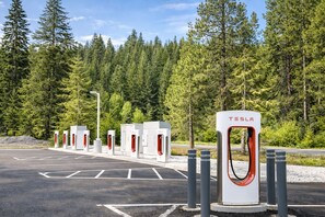 Estação de carregamento para veículos elétricos Tesla em área arborizada, com várias unidades de carregamento.
