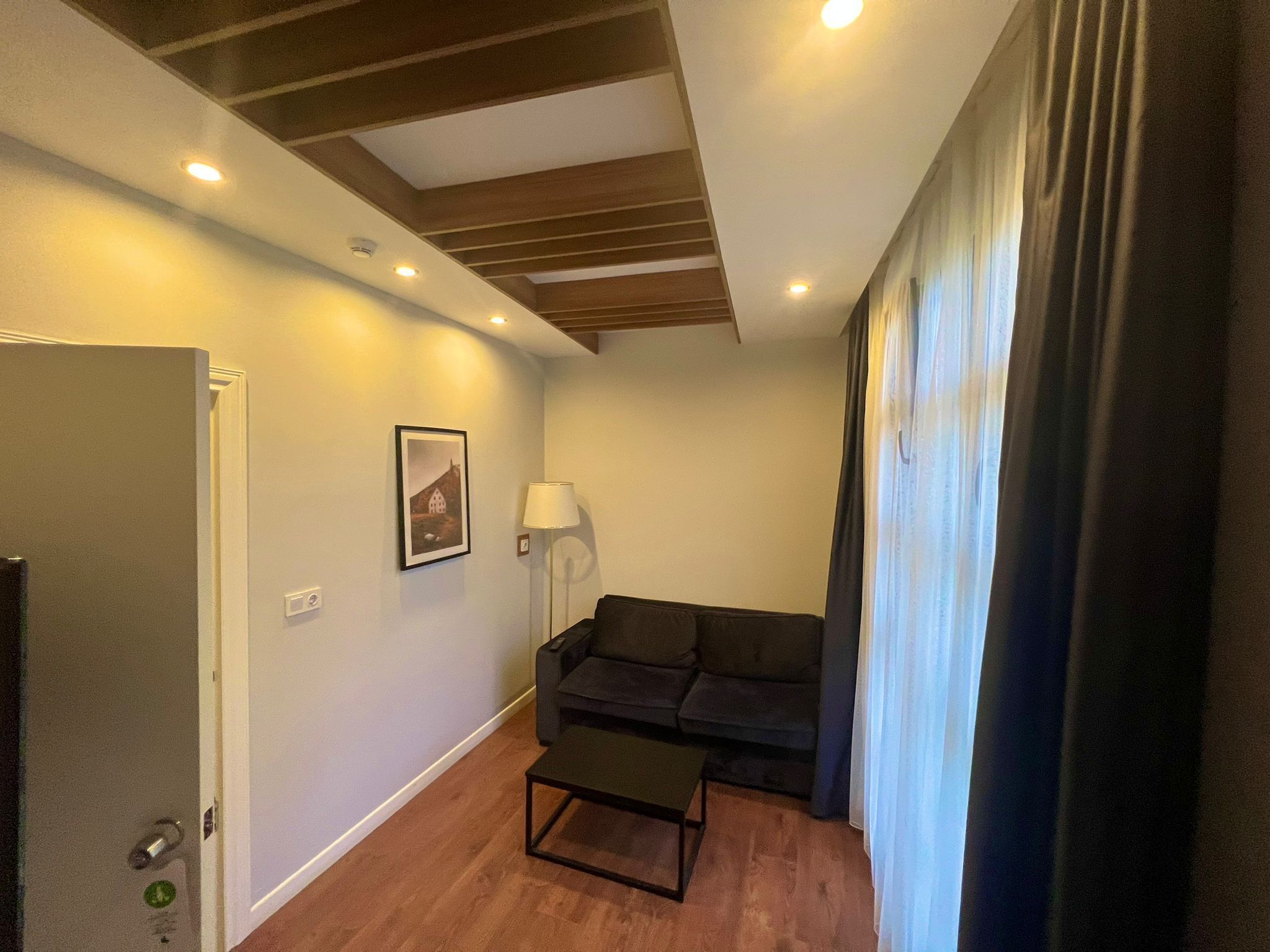 Quarto com sofá escuro, uma mesinha, luminária e quadro pendurado na parede.