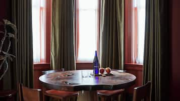 Uma sala de jantar com mesa redonda, quatro cadeiras, luminária pendente e janela com cortinas.