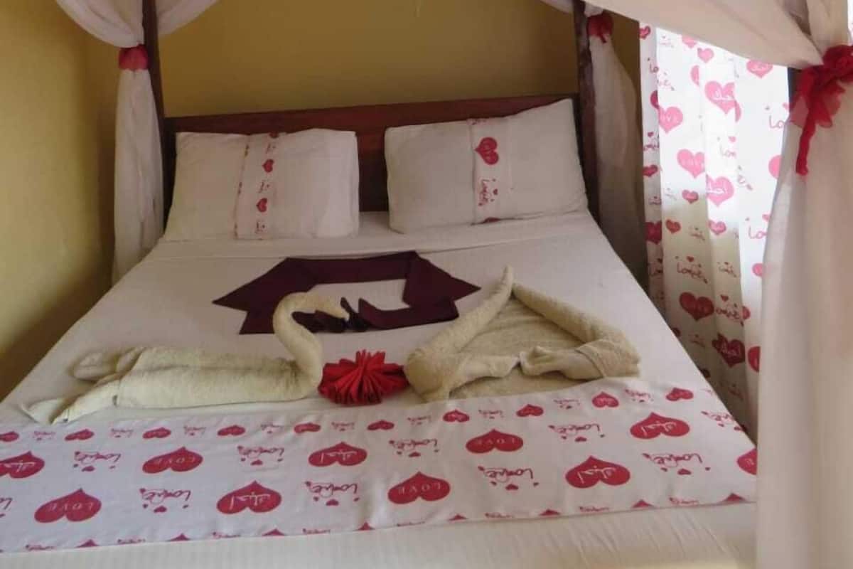Cama com dossel, roupa de cama branca com estampas de corações vermelhos e um objeto decorativo vermelho sobre a cama.