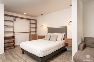 Quarto moderno com cama, mesas de cabeceira, guarda-roupa com prateleiras e uma cadeira.