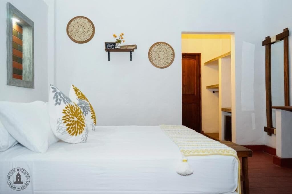 Quarto com cama, almofadas, mesa de cabeceira e detalhes decorativos nas paredes.