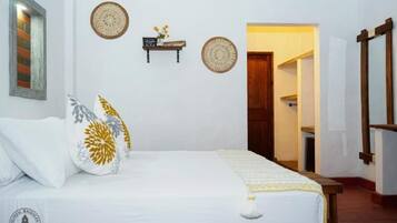 Quarto com cama, almofadas, mesa de cabeceira e detalhes decorativos nas paredes.