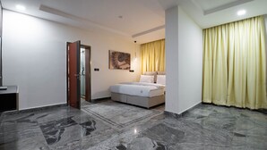 Quarto de hotel com cama, porta, quadro e cortina.