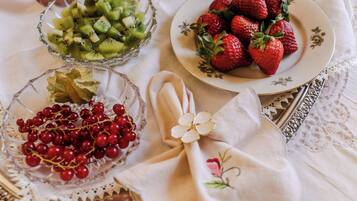 Uma mesa com três tigelas de vidro contendo frutas variadas, um prato de morangos e uma toalha de renda.