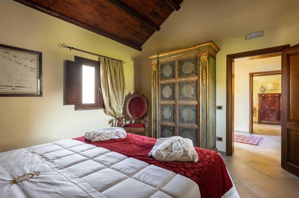 Quarto com cama grande, teto de madeira, guarda-roupa e porta para outro cômodo.