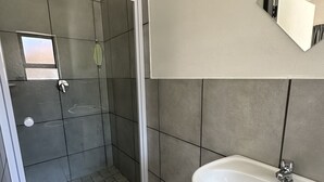 Um banheiro moderno com chuveiro em box de vidro, pia branca e paredes revestidas com azulejos.