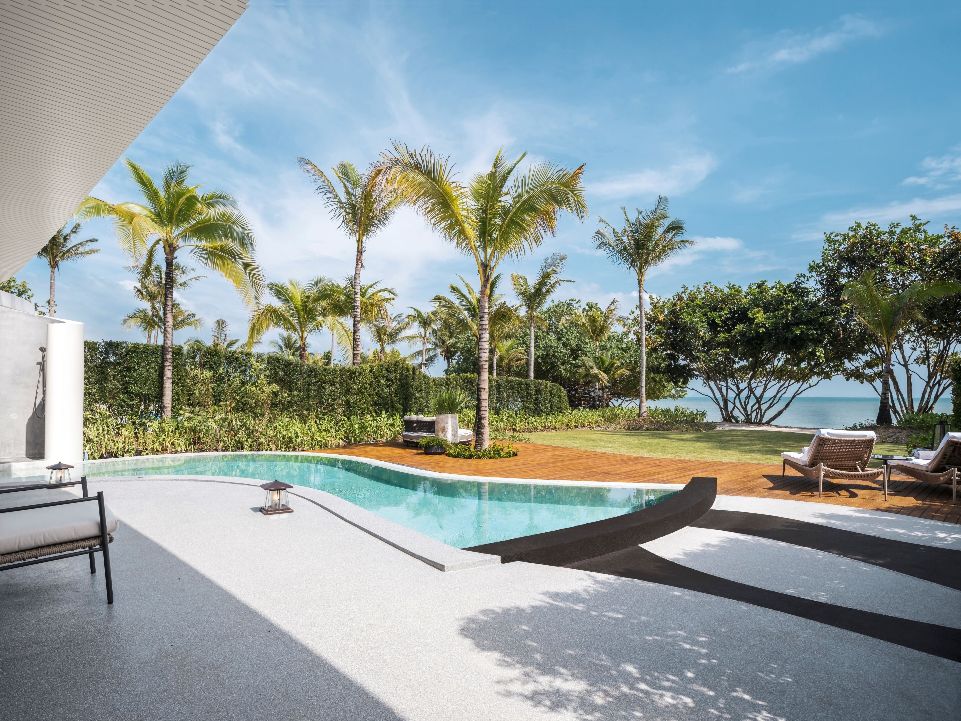 Uma área moderna de piscina ao ar livre com vista para o oceano, rodeada por palmeiras e um jardim bem cuidado.