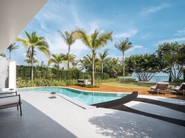 Uma área moderna de piscina ao ar livre com vista para o oceano, rodeada por palmeiras e um jardim bem cuidado.